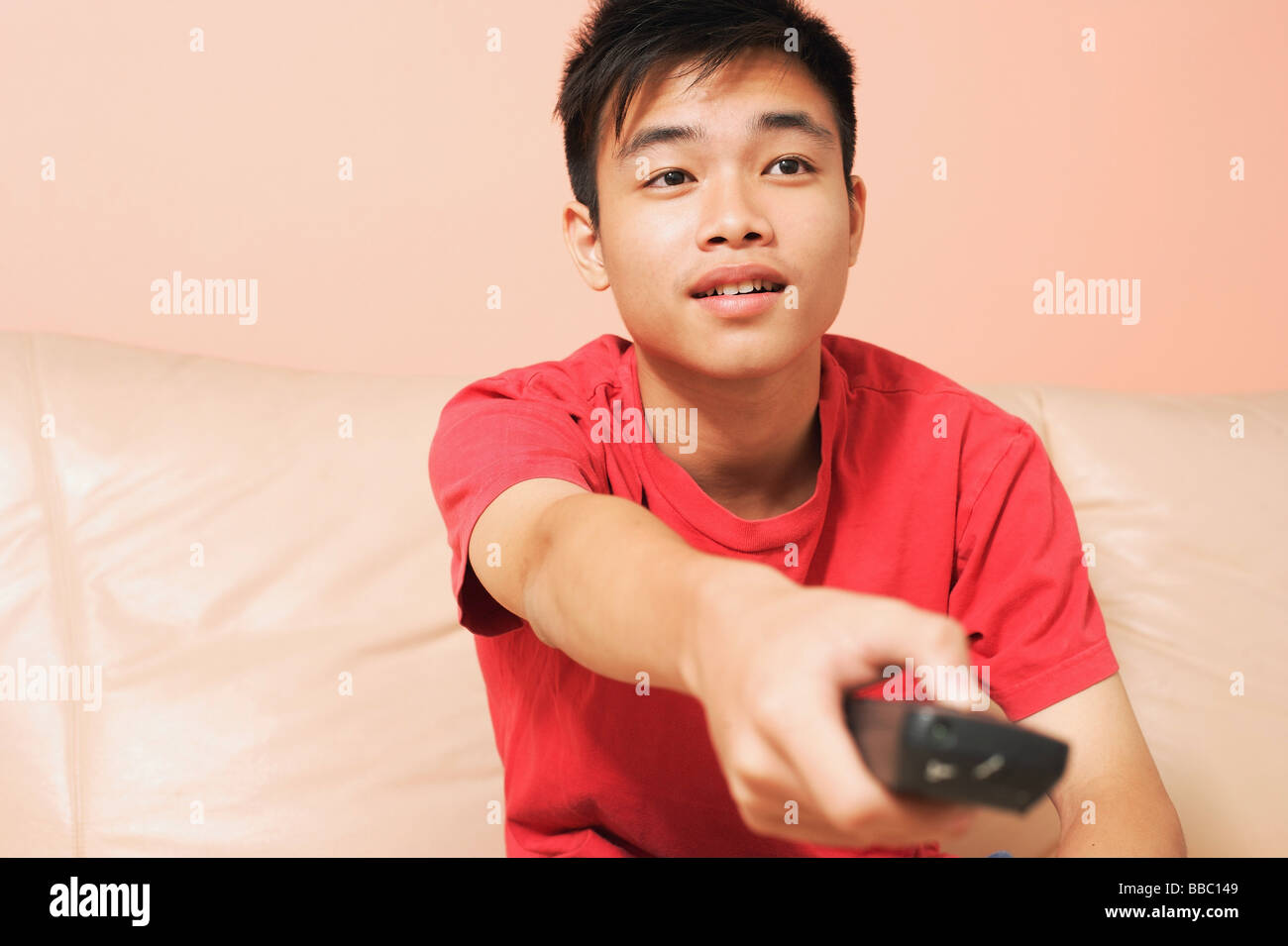 Teenage boy sitting on sofa, holding remote control forward Stock Photo ...