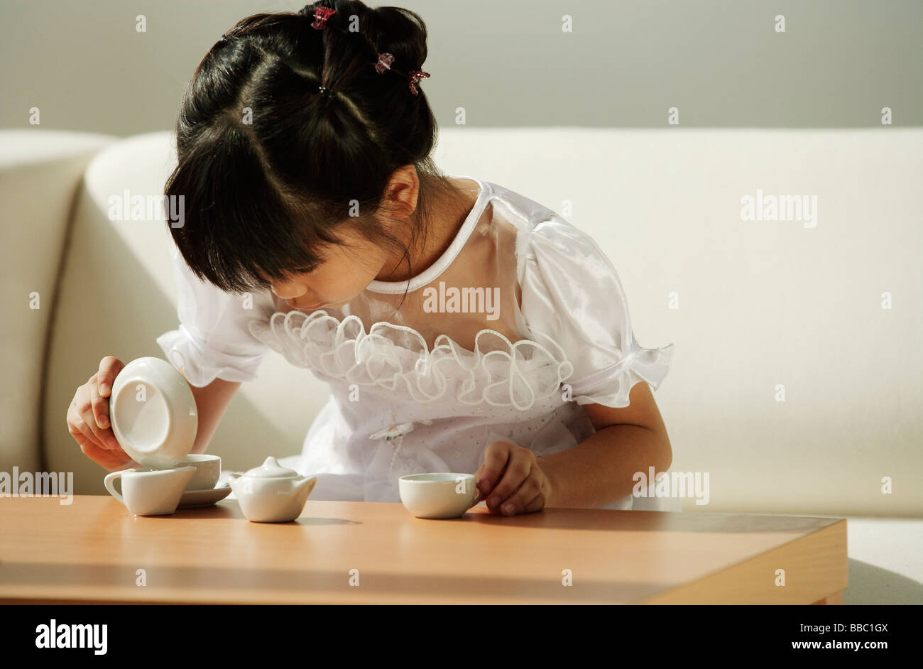 Girl in white dress playing with tea cups Stock Photo - Alamy