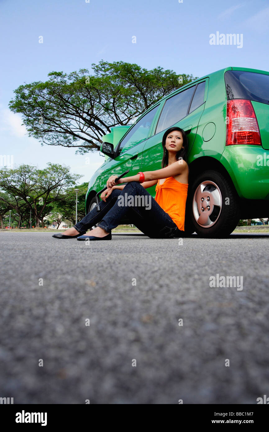 A young woman sits on the ground leaning against a car Stock Photo - Alamy