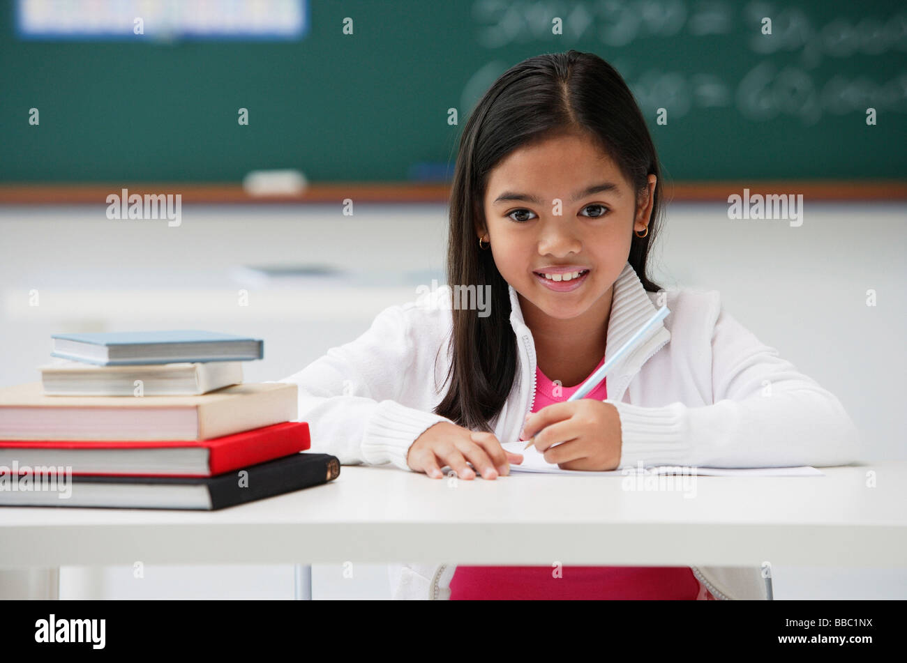 Girl with pen sitting at school desk smiling at camera Stock Photo - Alamy