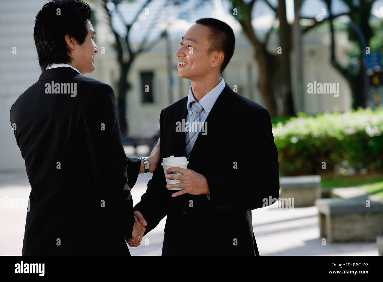 Two men wearing suits greet each other and shake hands in the park ...