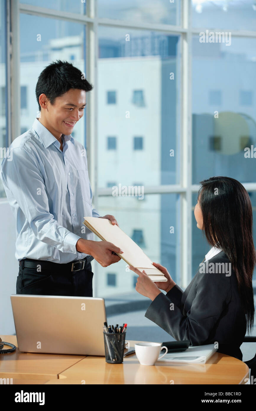Two colleagues smile at each other as they exchange documents Stock ...
