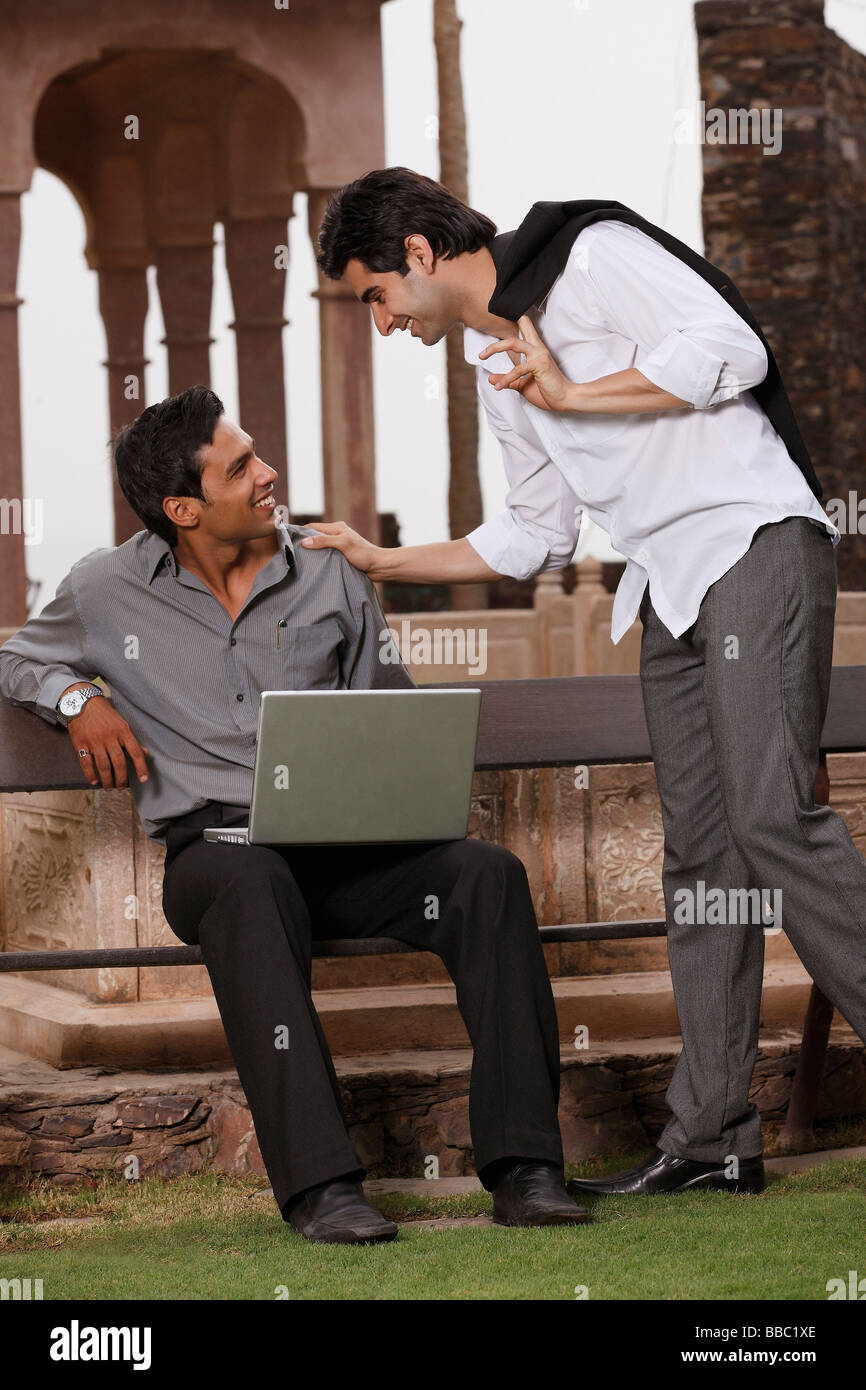 men talking outside, one working at laptop computer Stock Photo - Alamy