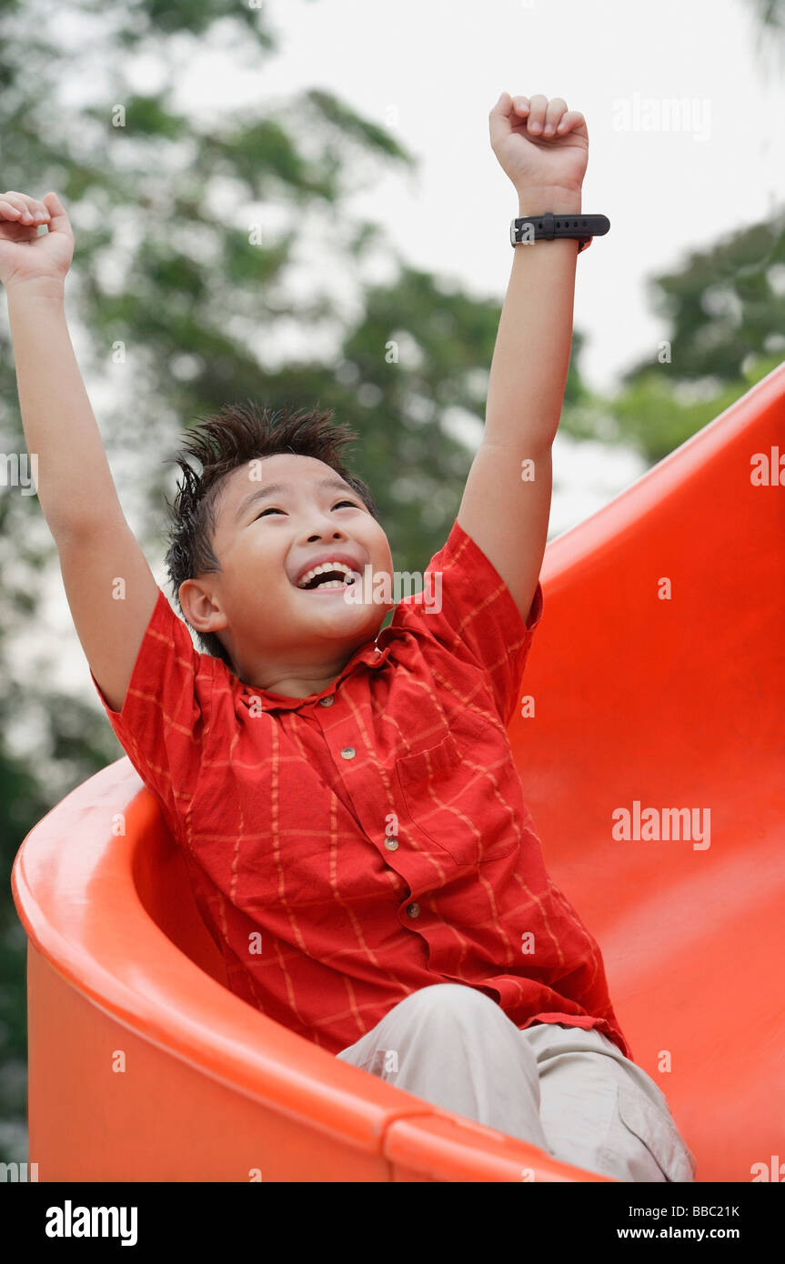 Boy coming down playground slide, arms outstretched, smiling, looking ...