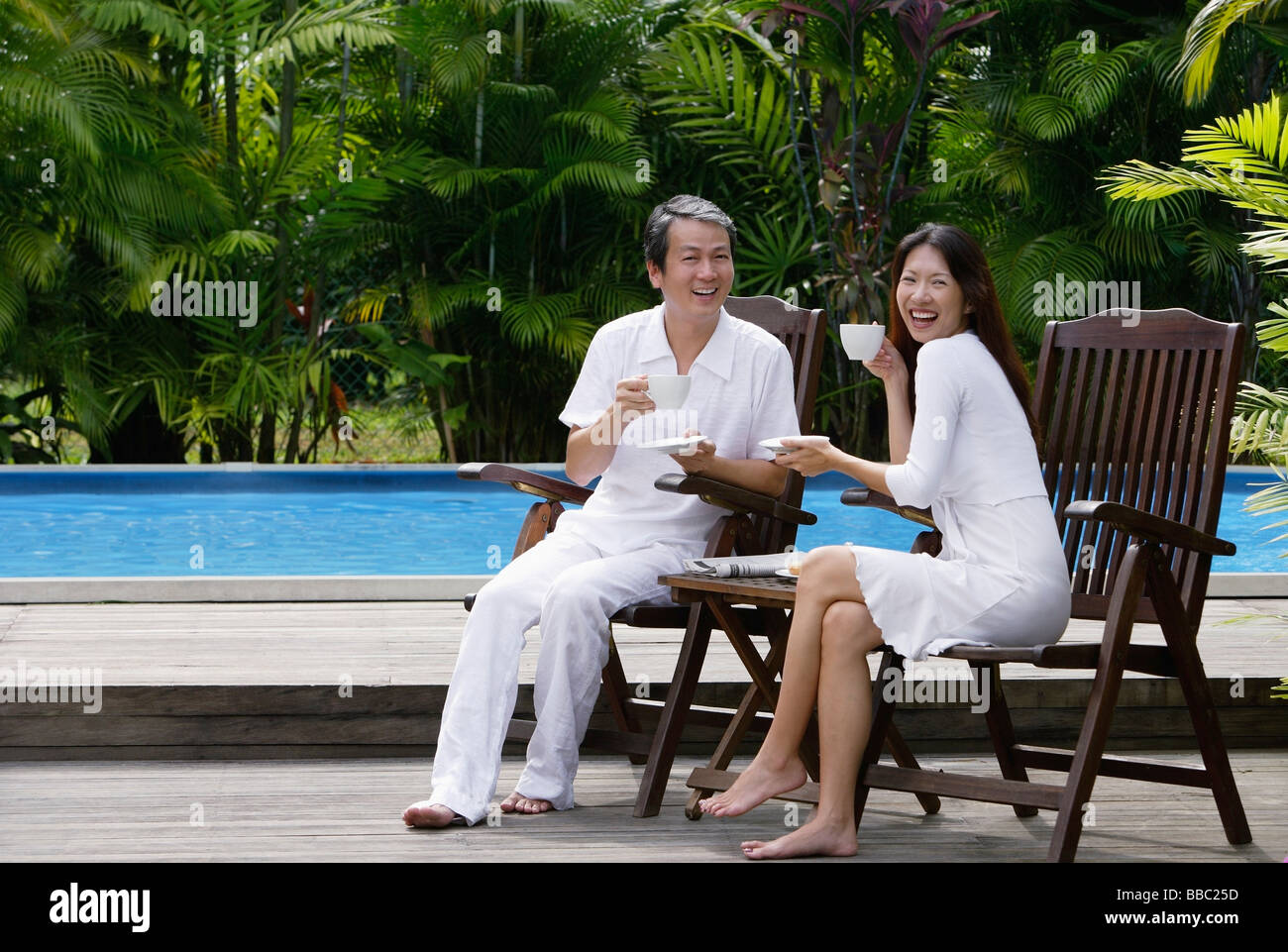 Couple sitting outdoors by swimming pool, having drinks Stock Photo - Alamy