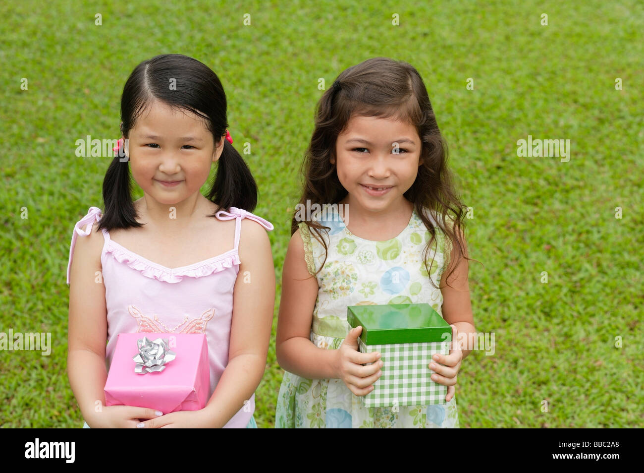 Two girls holding gift boxes, standing side by side, smiling at camera ...