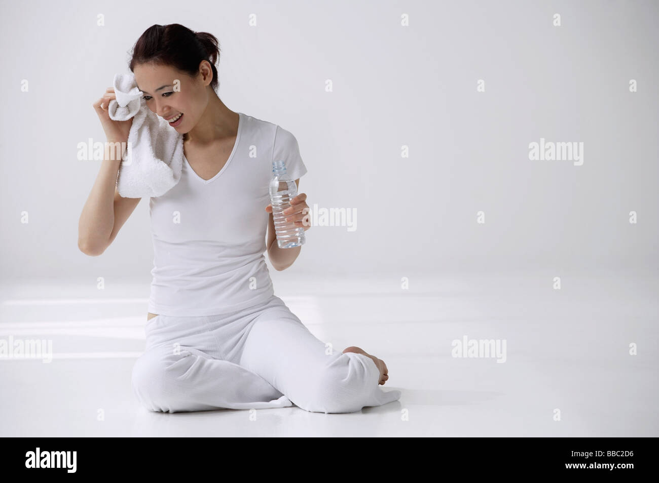 Woman sitting on floor with water bottle and towel, drying off sweat on ...