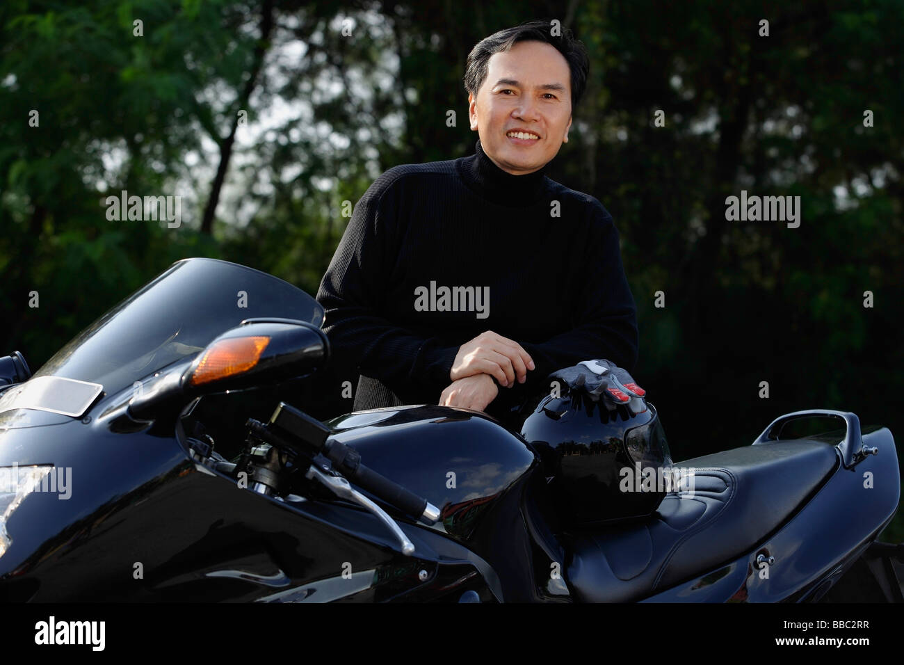 Man standing by black motorcycle, smiling at camera Stock Photo - Alamy