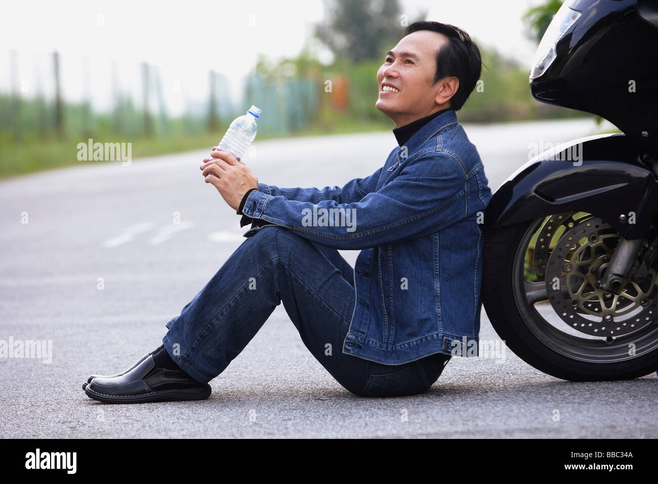 Man leaning against motorcycle, sitting on road drinking water Stock ...