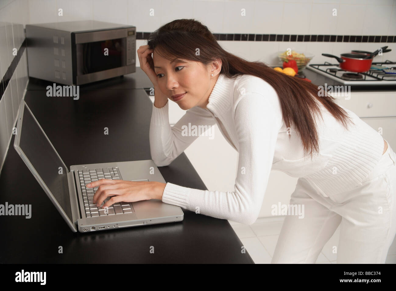 Woman leaning on counter, looking at laptop / computer Stock Photo - Alamy