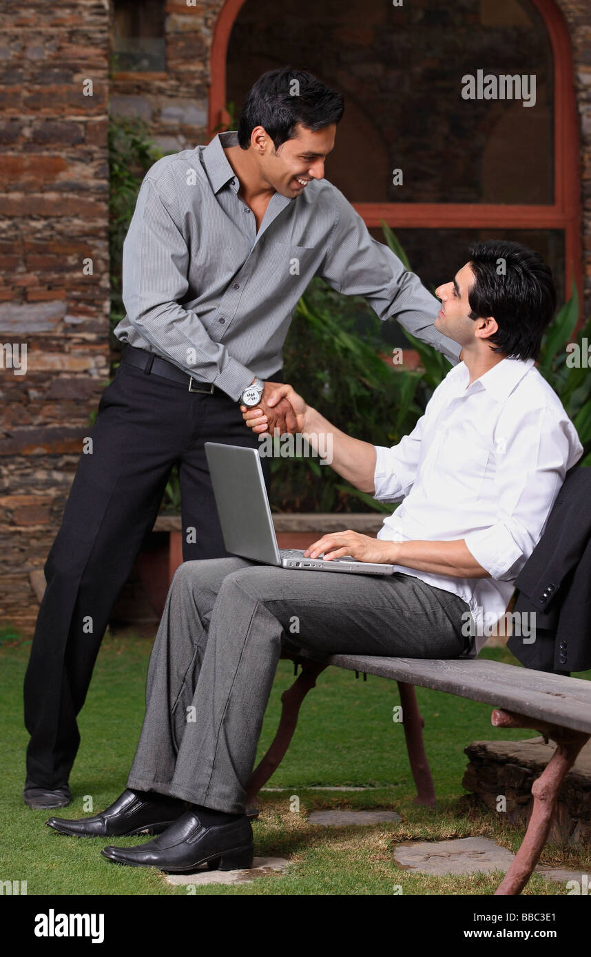businessmen shaking, one at laptop computer Stock Photo - Alamy