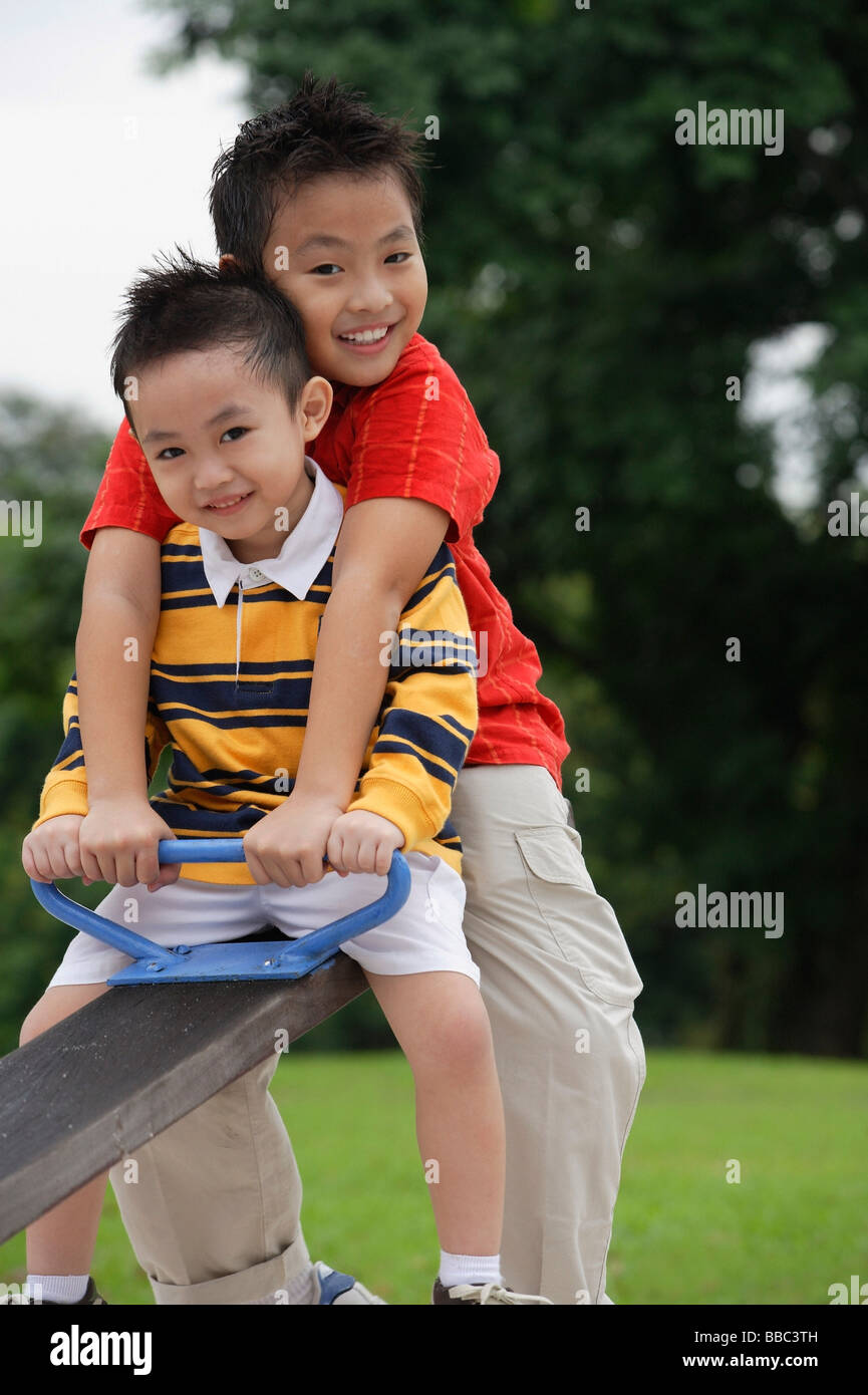 Two brothers sitting on See-Saw, smiling at camera Stock Photo - Alamy