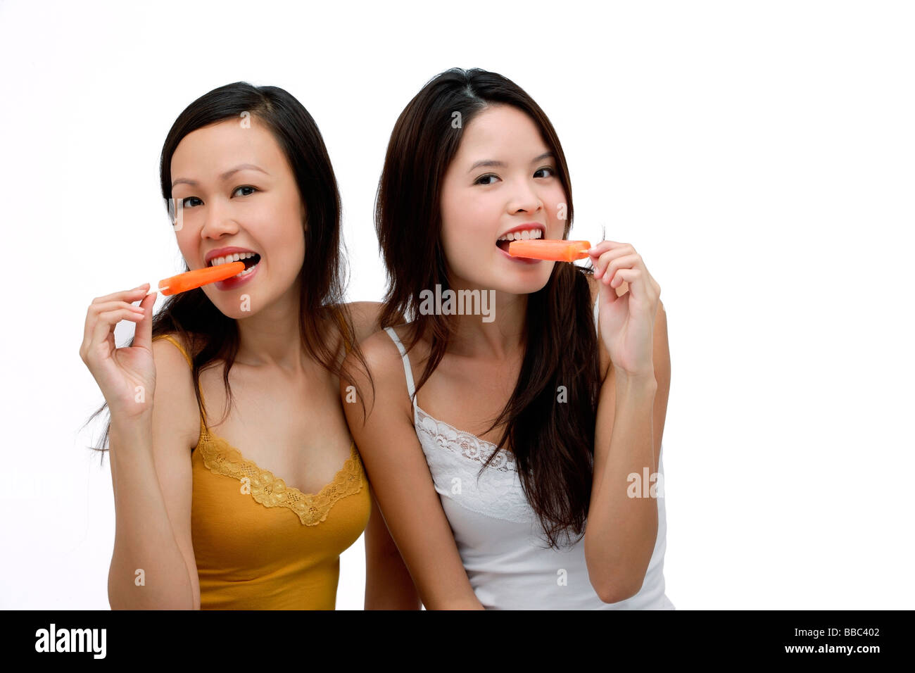 Two young women biting into Popsicle, looking at camera Stock Photo - Alamy