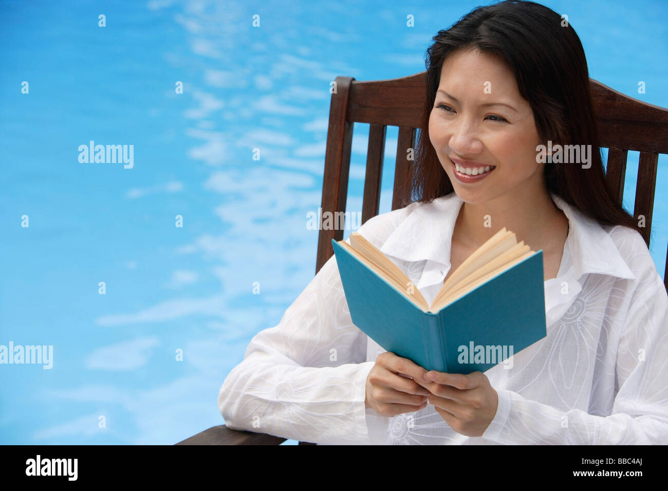 Woman by swimming pool, reading a book, looking away Stock Photo - Alamy