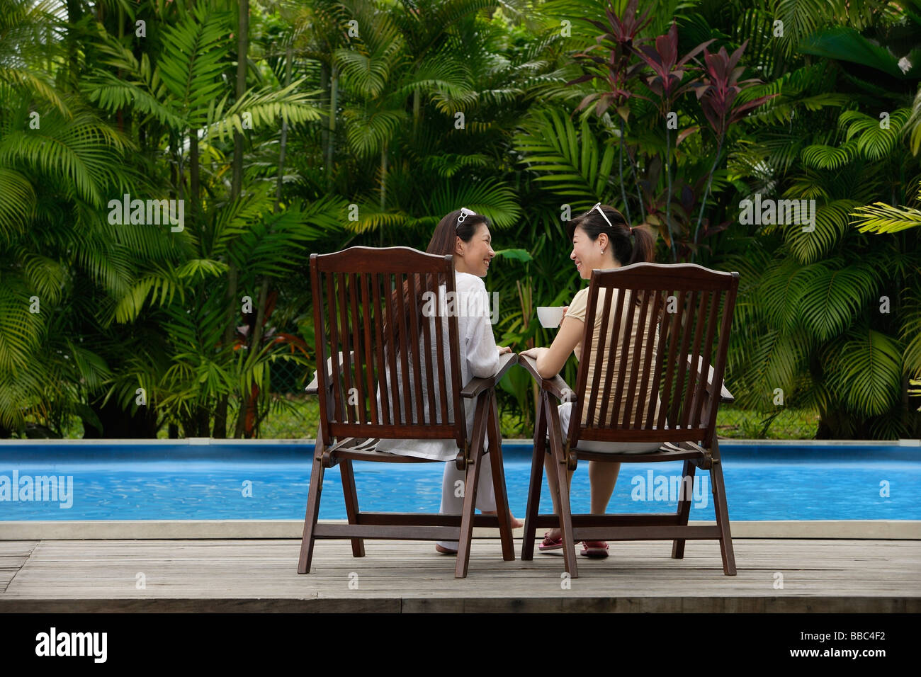 Two women sitting next to swimming pool, drinking and talking Stock ...