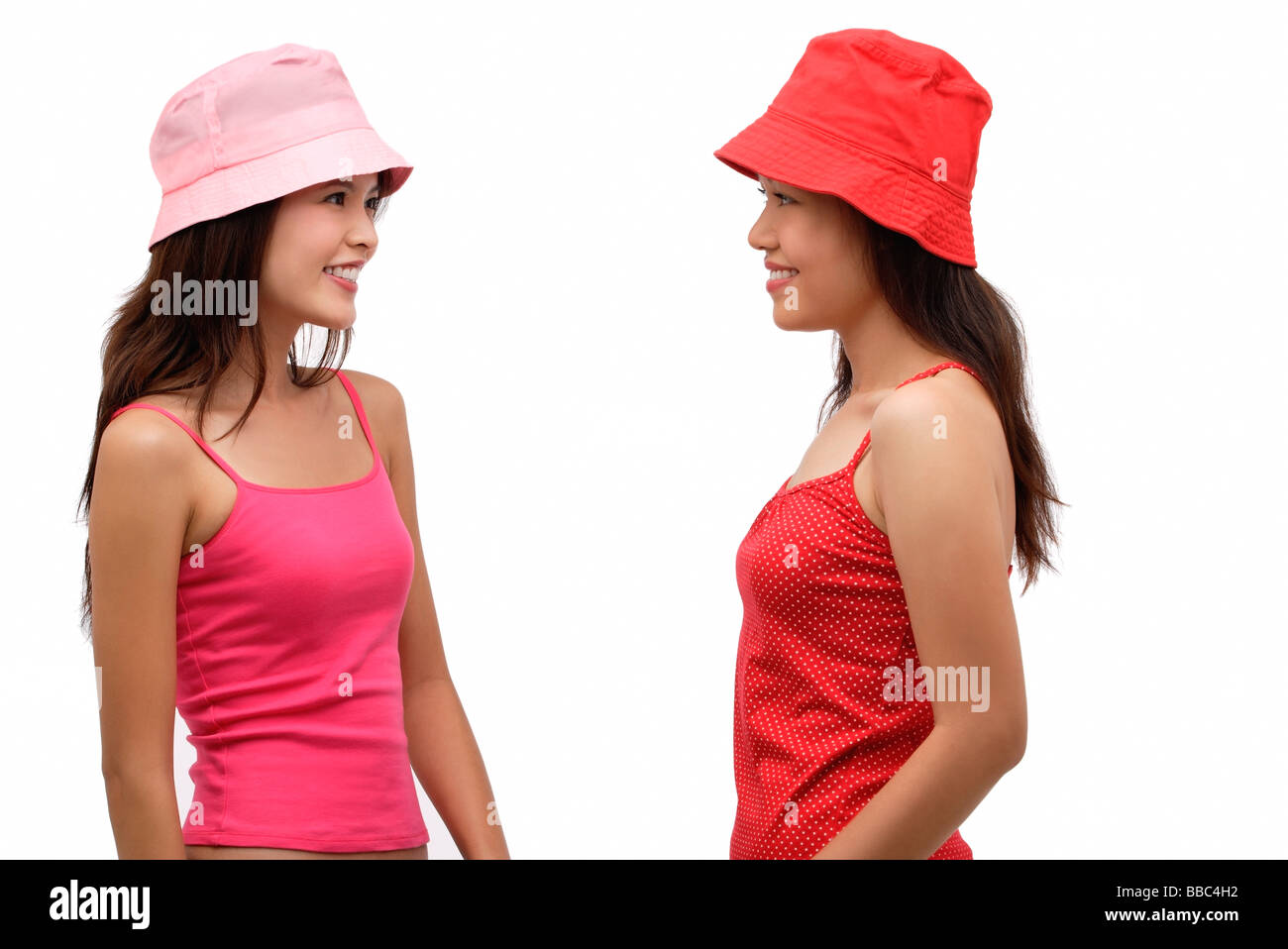 Two young women wearing pink and red hats, looking at each other Stock ...