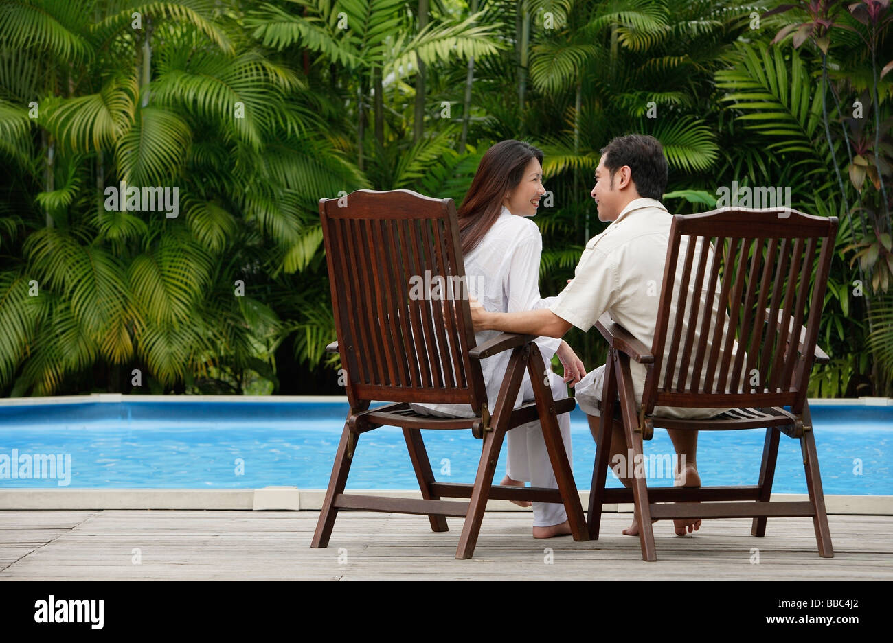 Couple sitting by swimming pool, looking at each other, rear view Stock ...