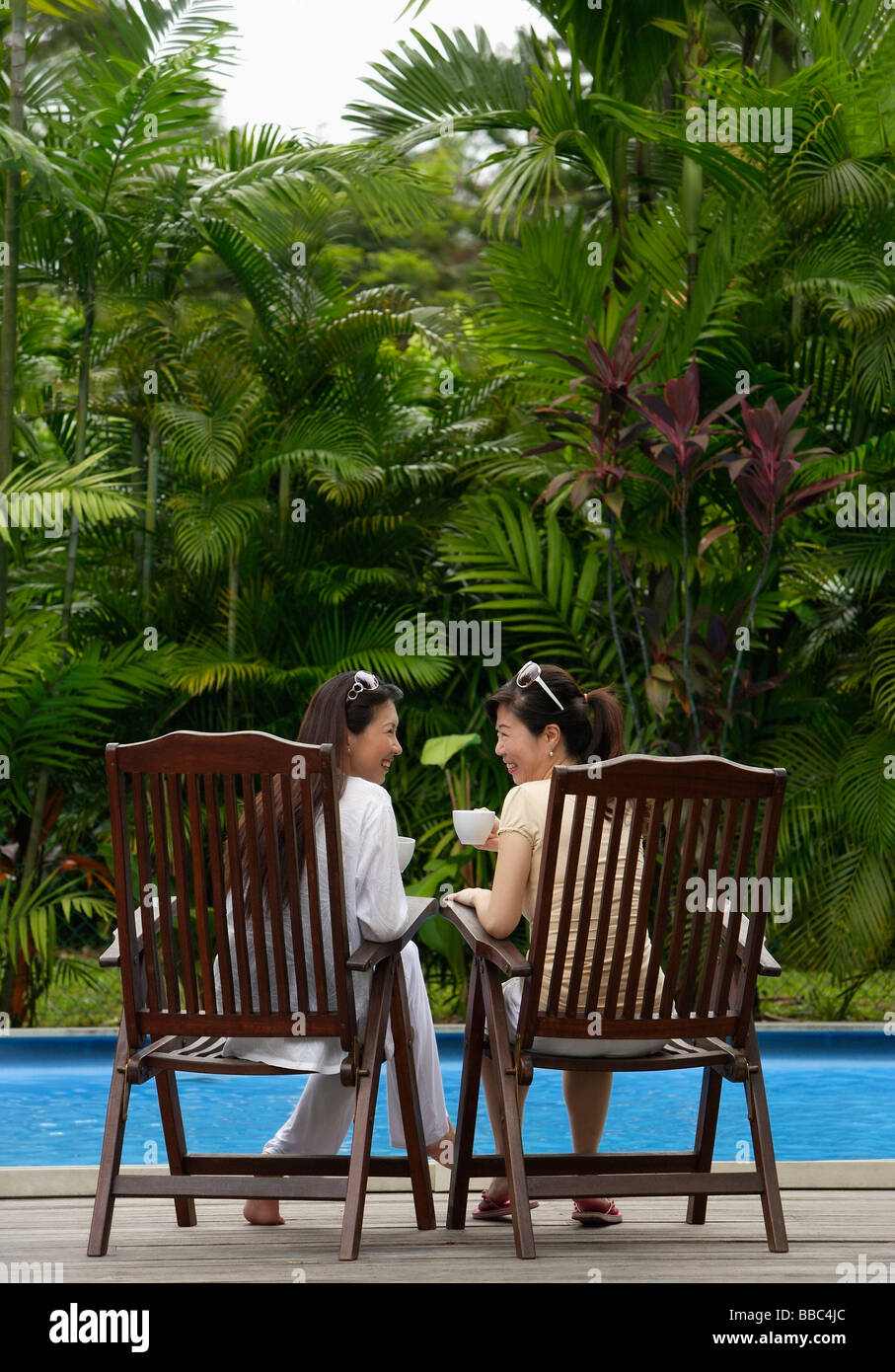 Two women sitting and talking by swimming pool Stock Photo - Alamy