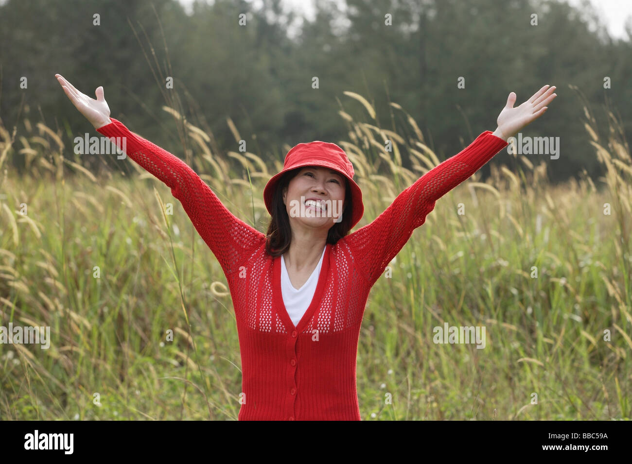 Woman standing in tall grass, arms raised to sky, happy, smiling Stock ...