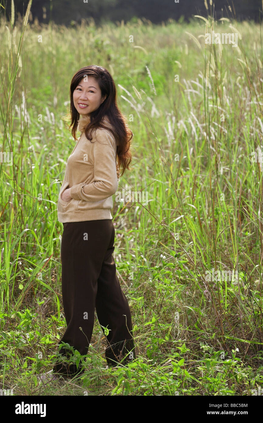 Woman standing in tall grass, looking over shoulder at camera Stock ...