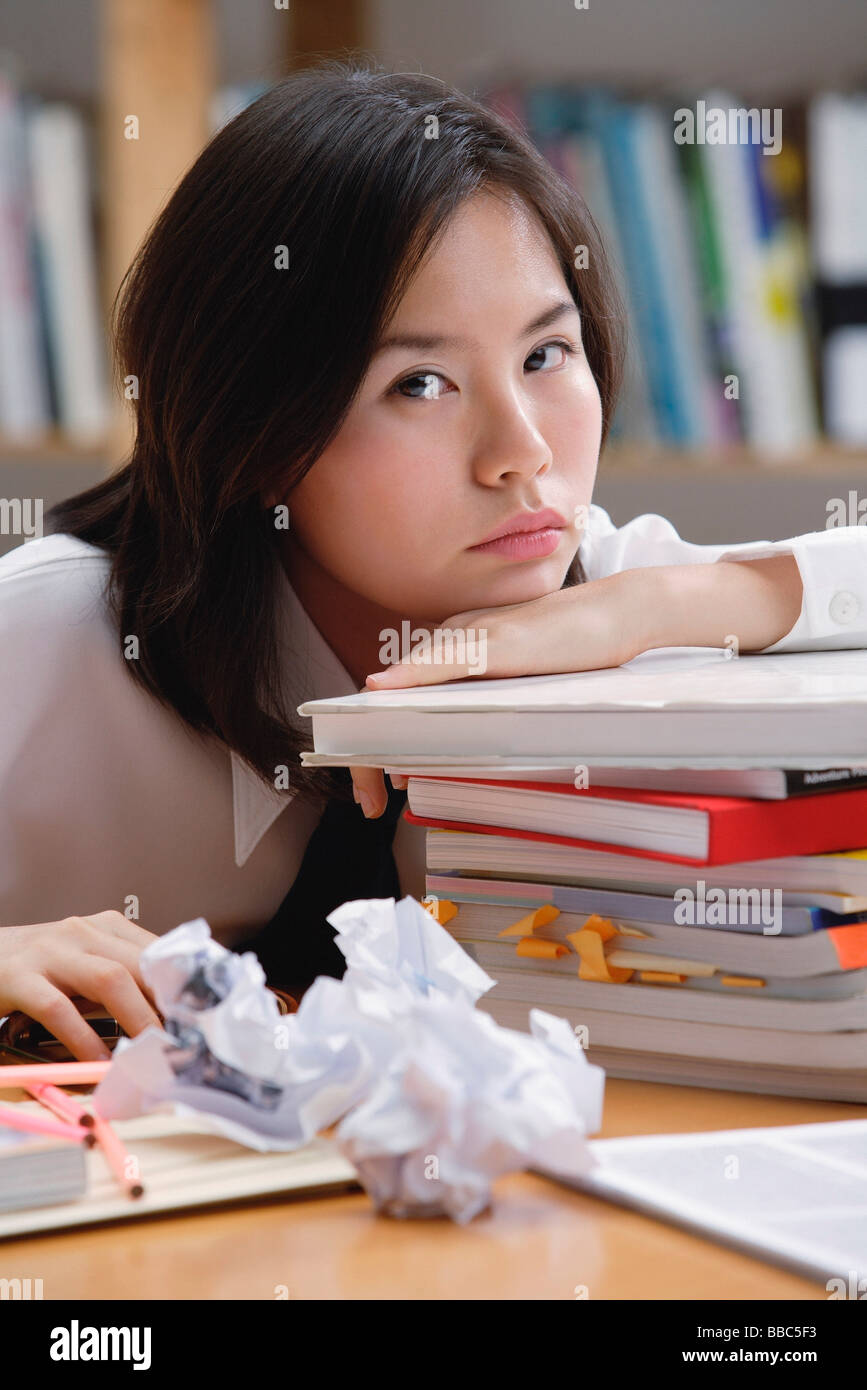 Young woman in library, leaning on books, sad expression Stock Photo ...