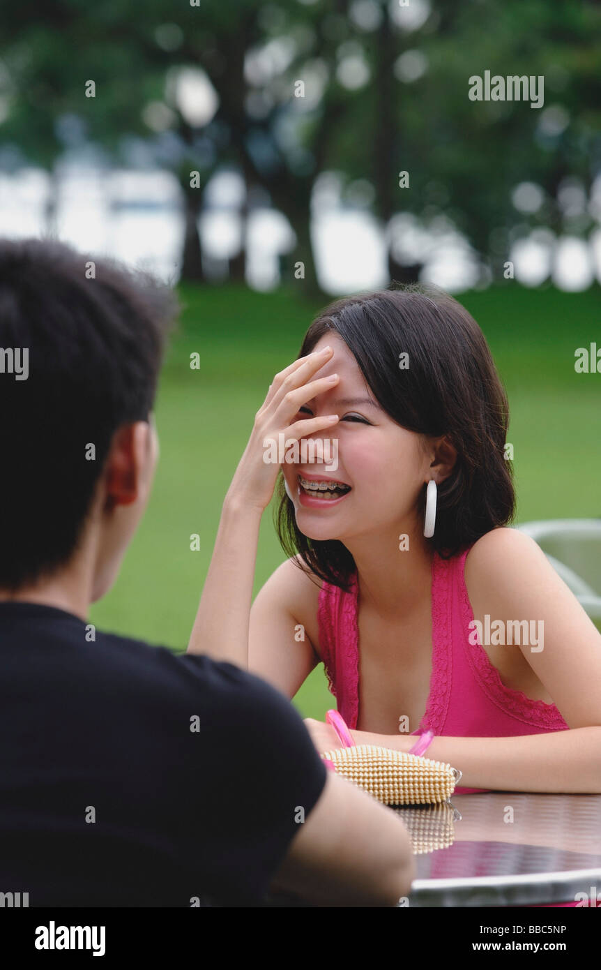 Young woman with hand over face, smiling at man sitting opposite from ...