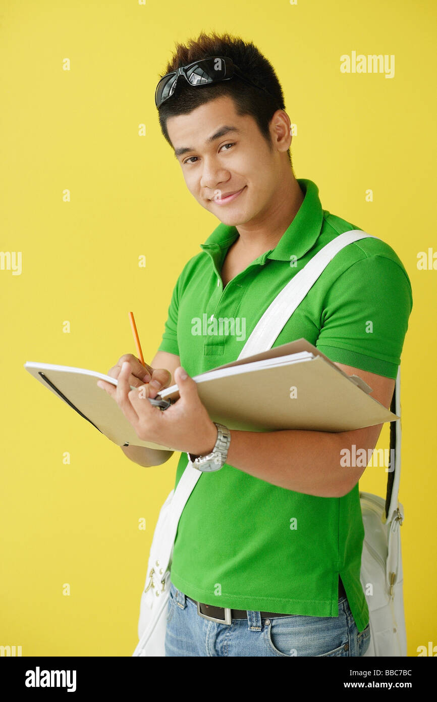Man standing against yellow background, writing in notebook, looking at ...
