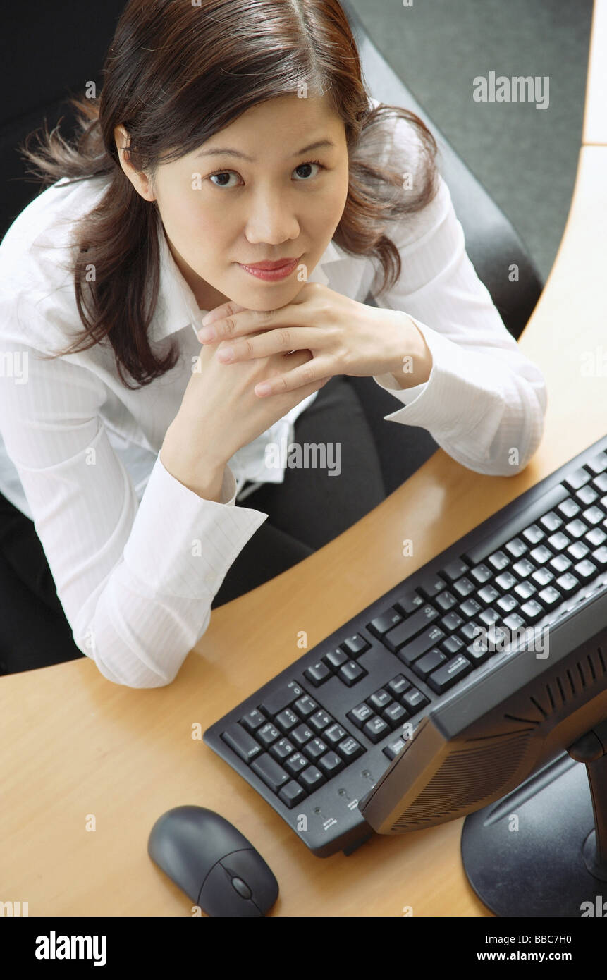 Businesswoman sitting in office cubicle, hands on chin, looking up at ...