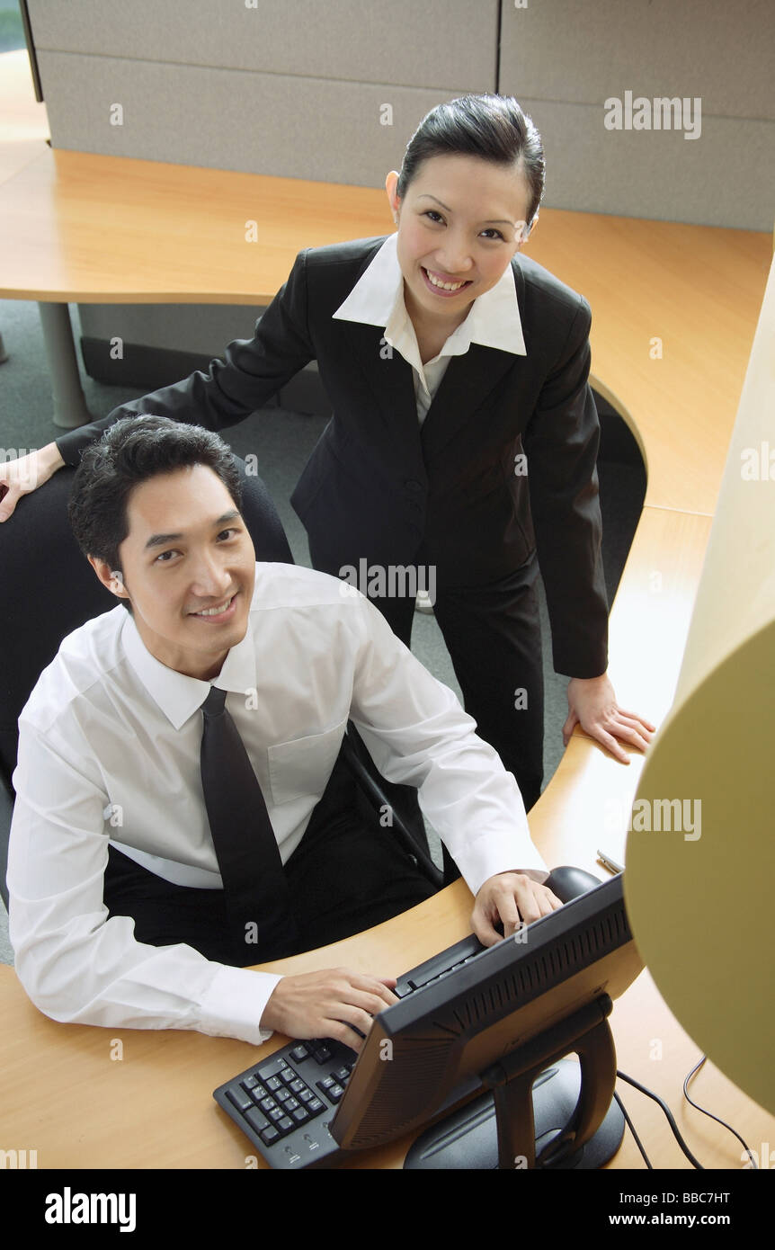 Businessman and woman in office cubicle, looking up at camera, smiling ...