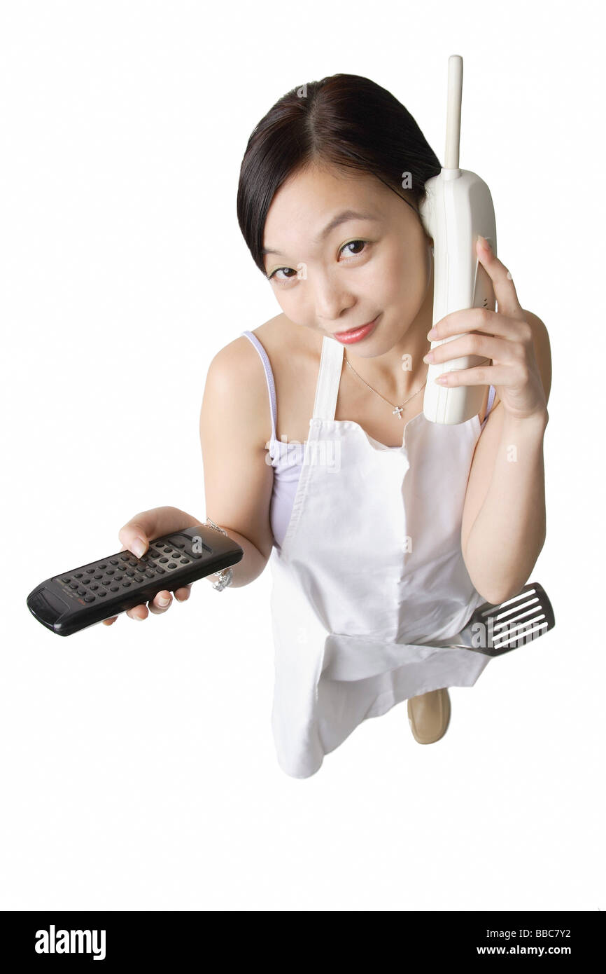 Woman in apron using cordless phone, holding remote control Stock Photo ...