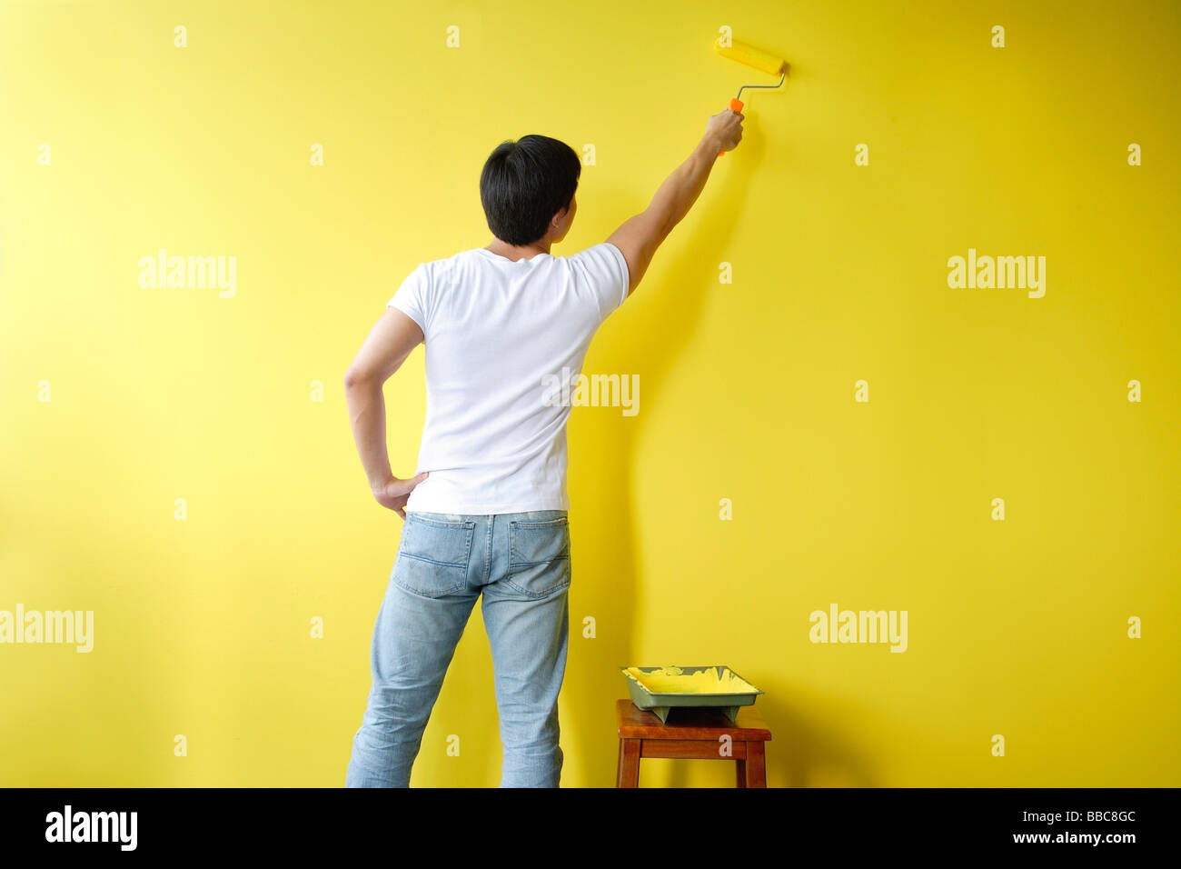 Man with paint roller, painting wall yellow Stock Photo - Alamy
