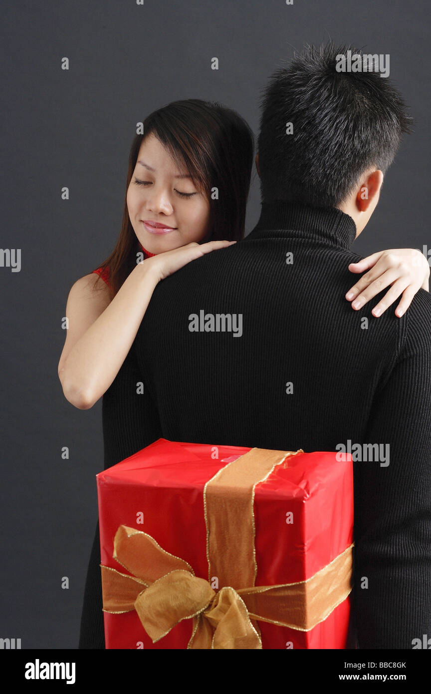 Man holding gift behind his back, woman embracing him Stock Photo - Alamy
