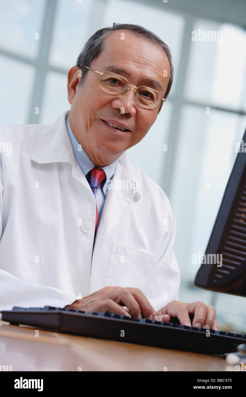 Doctor in office, using desktop computer, looking at camera Stock Photo ...