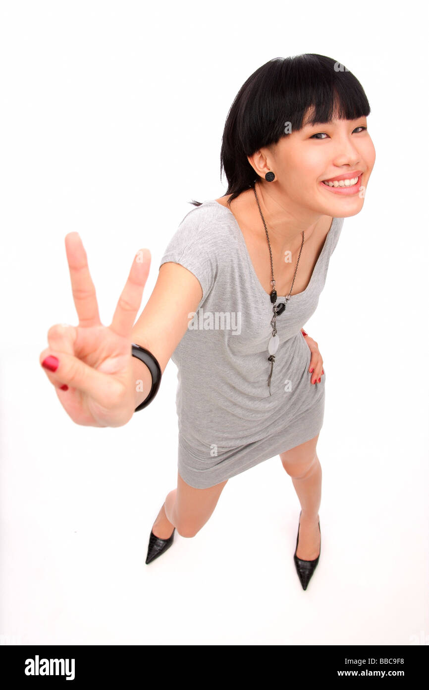 Young woman smiling up at camera, making peace sign Stock Photo - Alamy