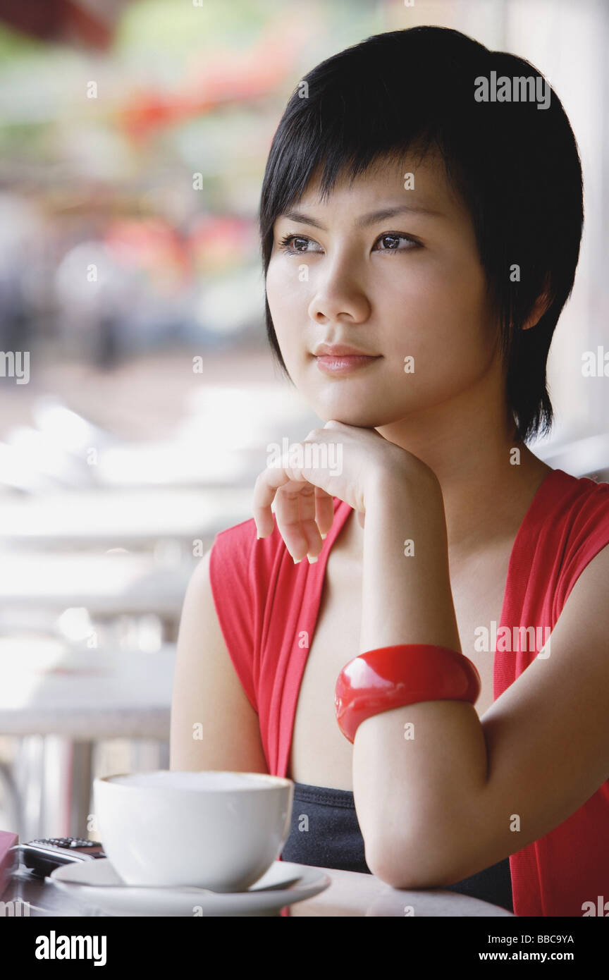 Woman with hand on chin, cup and saucer next to her Stock Photo - Alamy