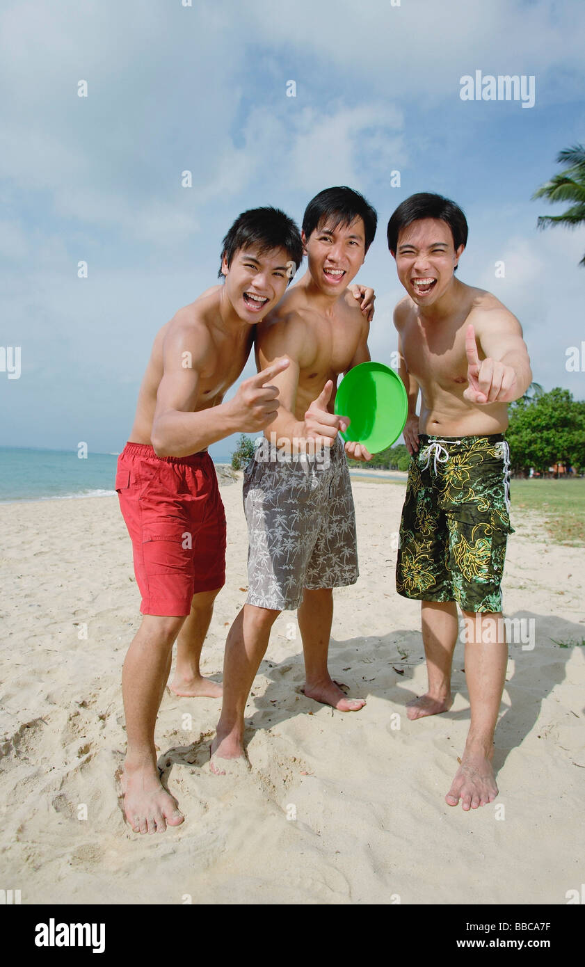Three men on beach, standing side by side, making hand sign Stock Photo ...