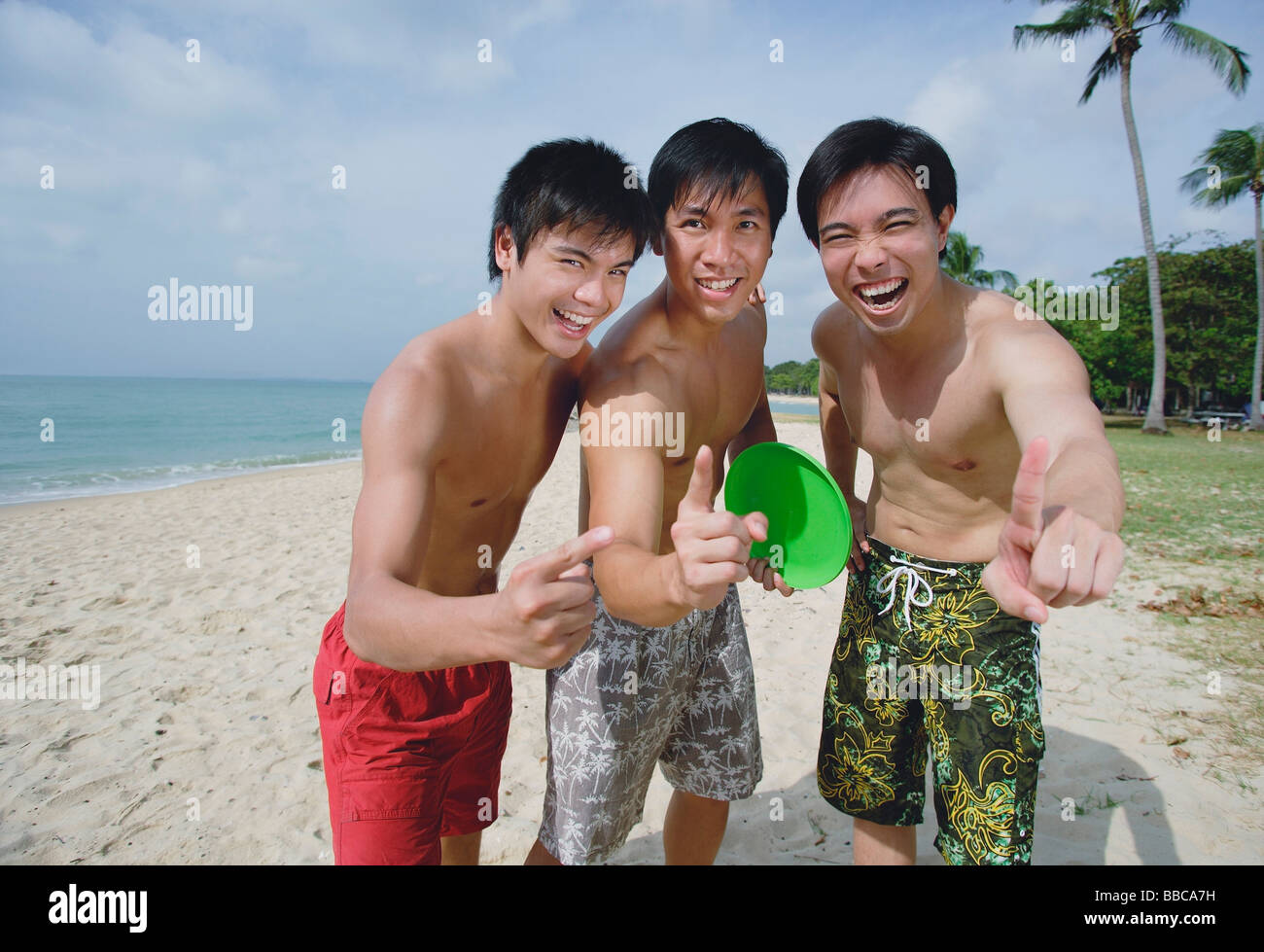 Men on beach, standing side by side, making hand sign Stock Photo - Alamy
