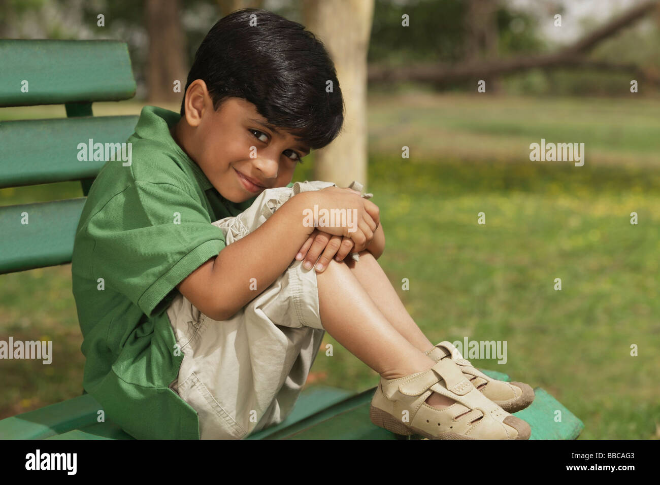 Little boy hugging knees on park bench Stock Photo - Alamy