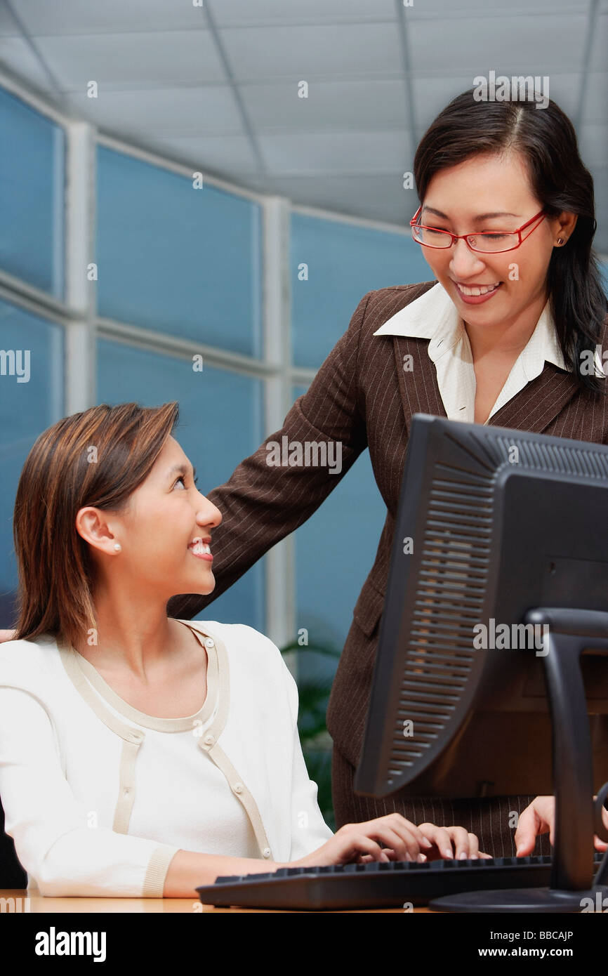 Female executive at computer, smiling at woman standing next to her ...