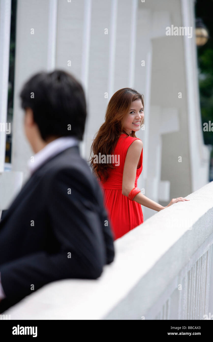 Man leaning on bridge railing, woman in background turning to look at ...