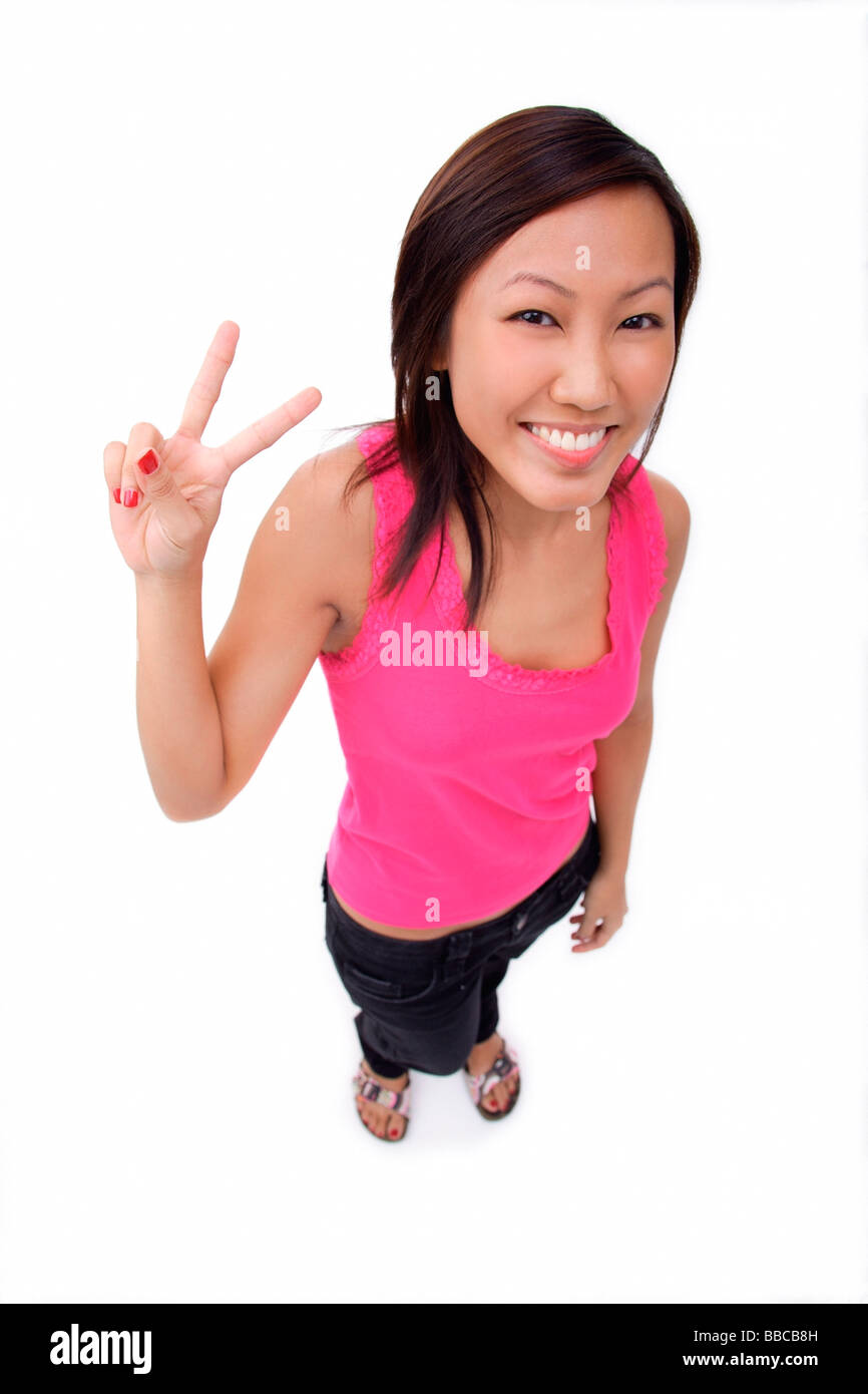 Young woman making peace sign, smiling up at camera Stock Photo - Alamy