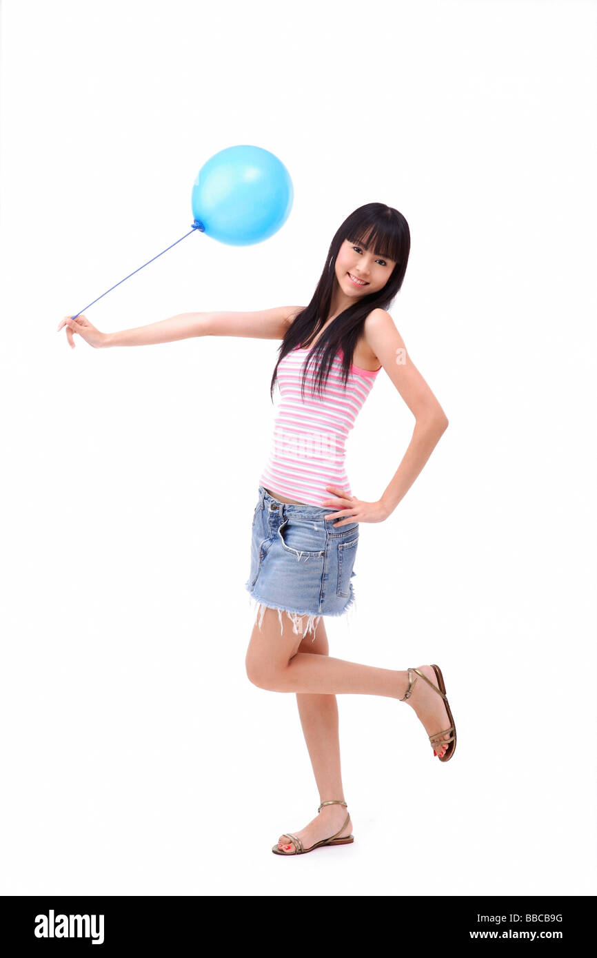 Young woman holding a blue balloon, standing on one leg Stock Photo - Alamy