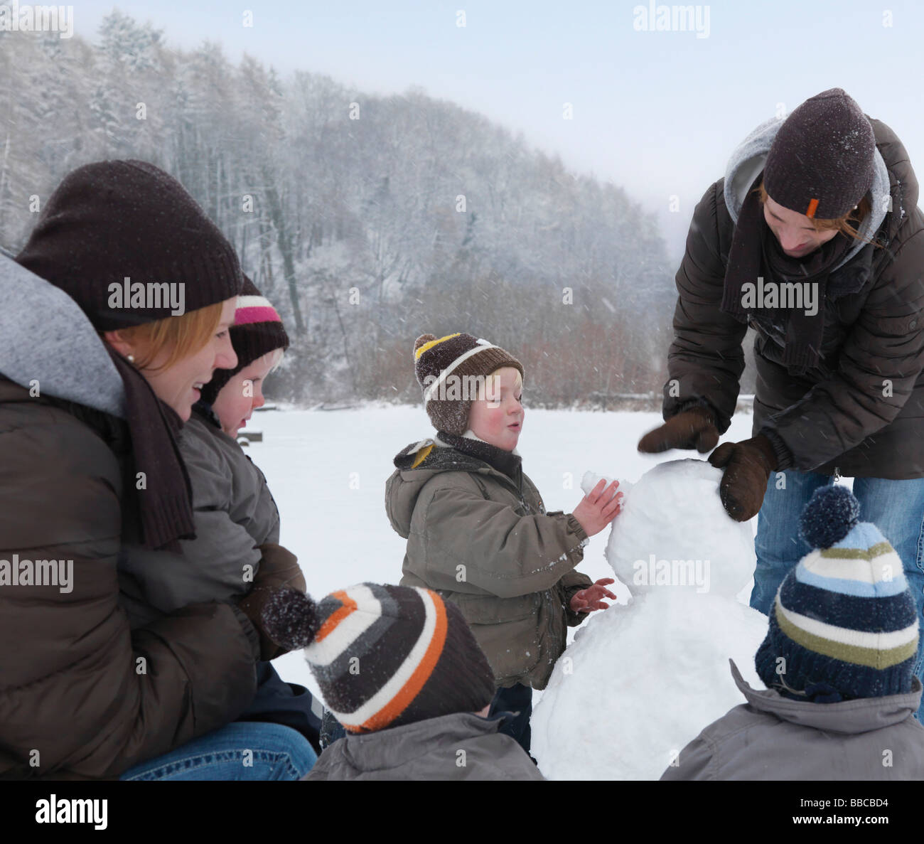 Women and children building snowman Stock Photo - Alamy