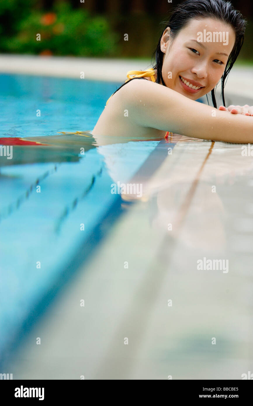 Woman leaning on the edge of swimming pool, smiling Stock Photo - Alamy
