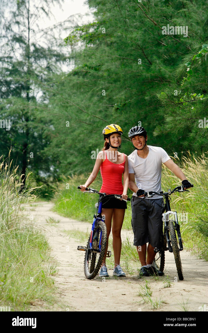 Couple standing with bicycles, smiling at camera Stock Photo - Alamy