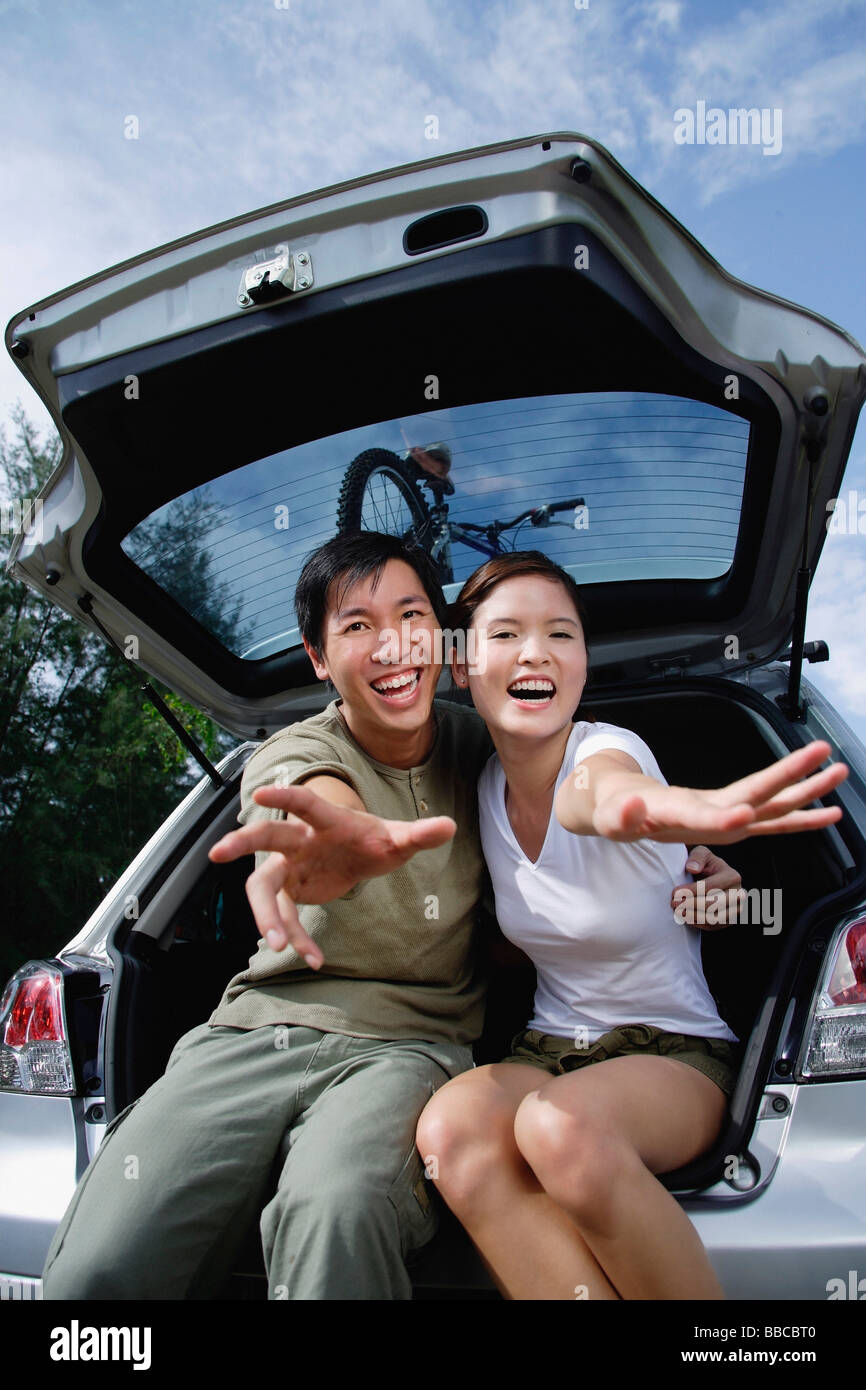 Couple sitting in boot of car, reaching towards camera Stock Photo - Alamy