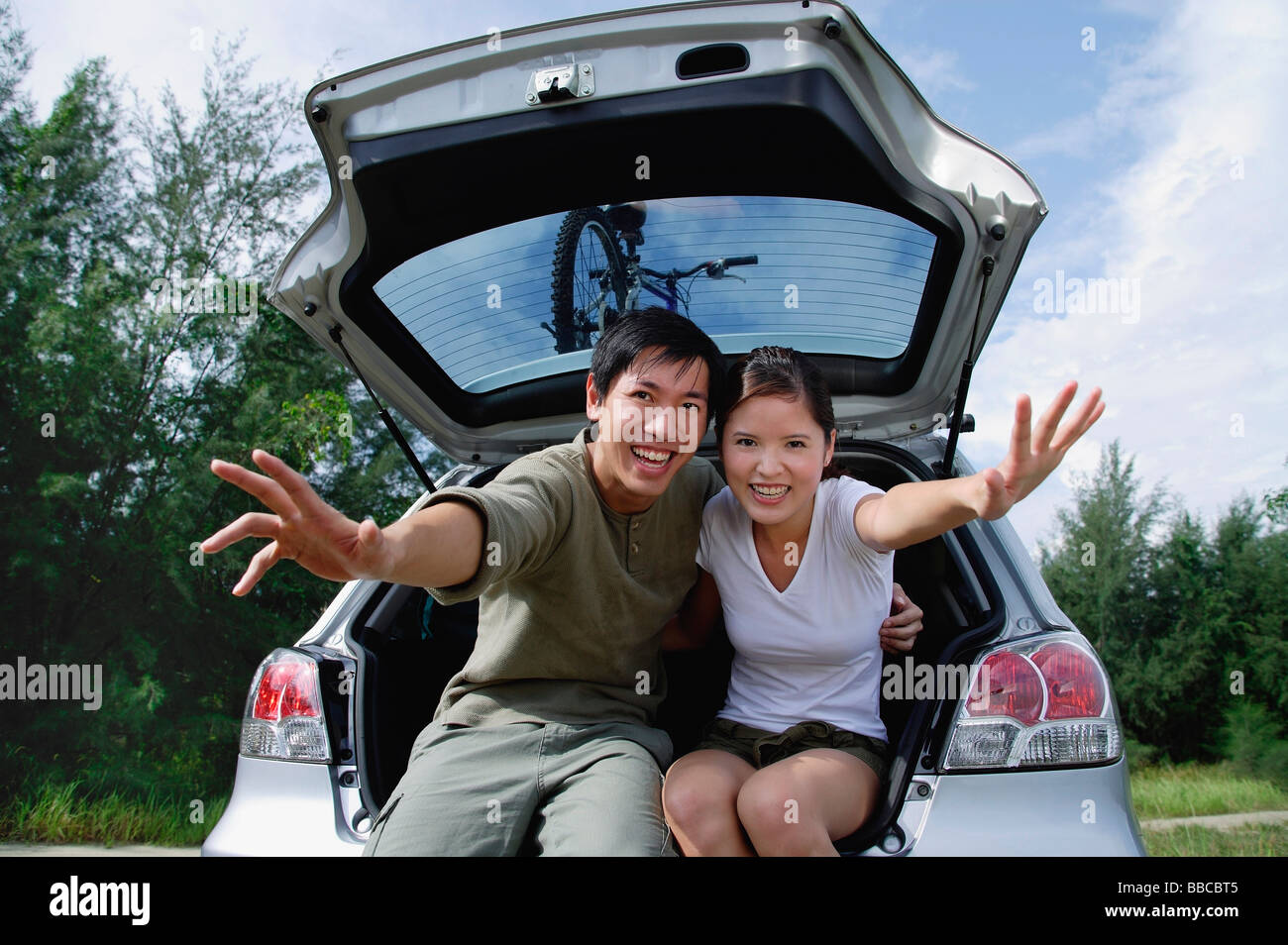 Couple sitting in boot of car, reaching towards camera, smiling Stock ...