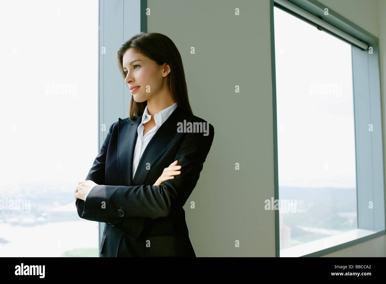 Businesswoman standing next to window in conference room, arms crossed ...