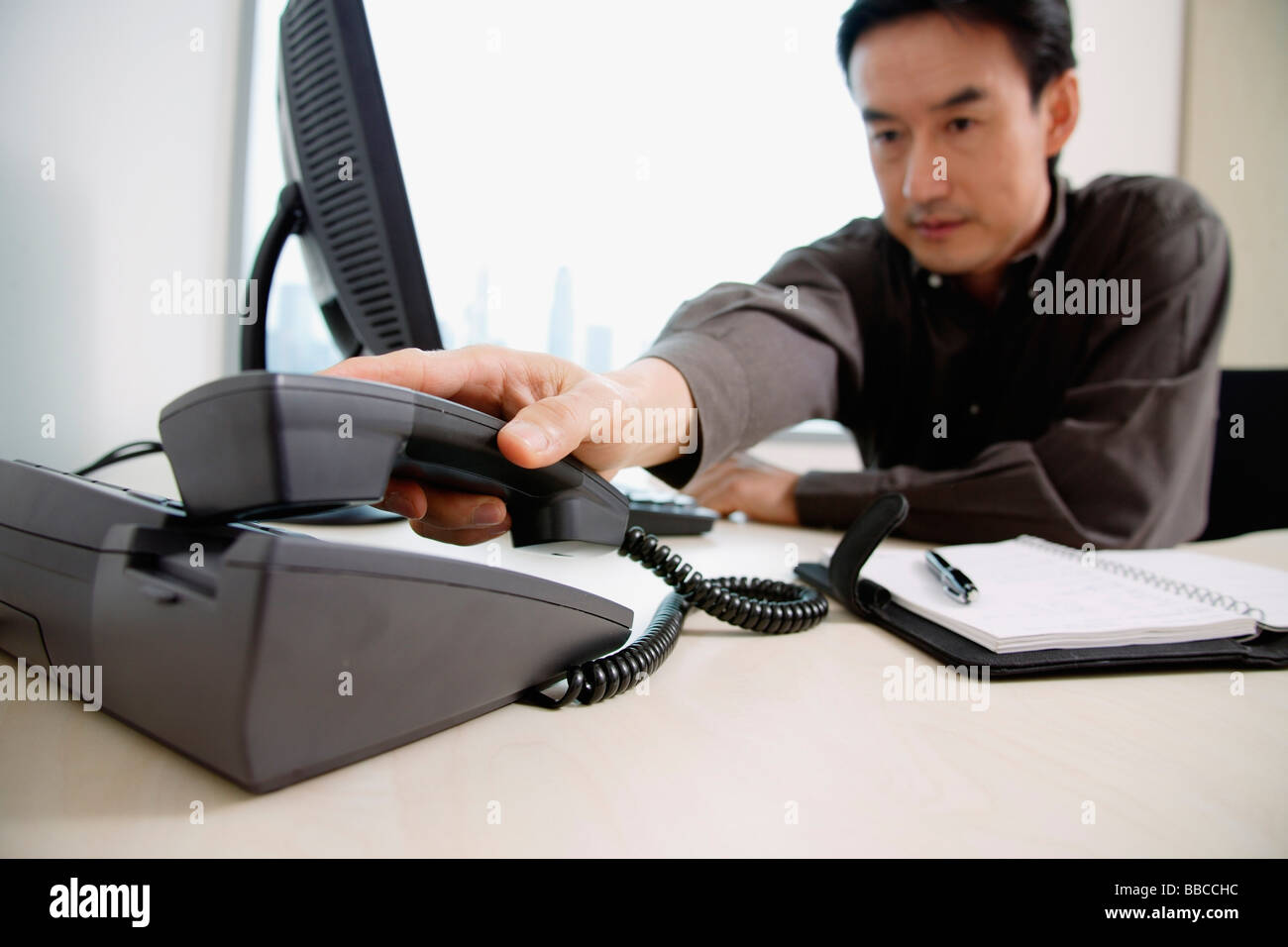 Male executive sitting at office desk, reaching for telephone Stock ...