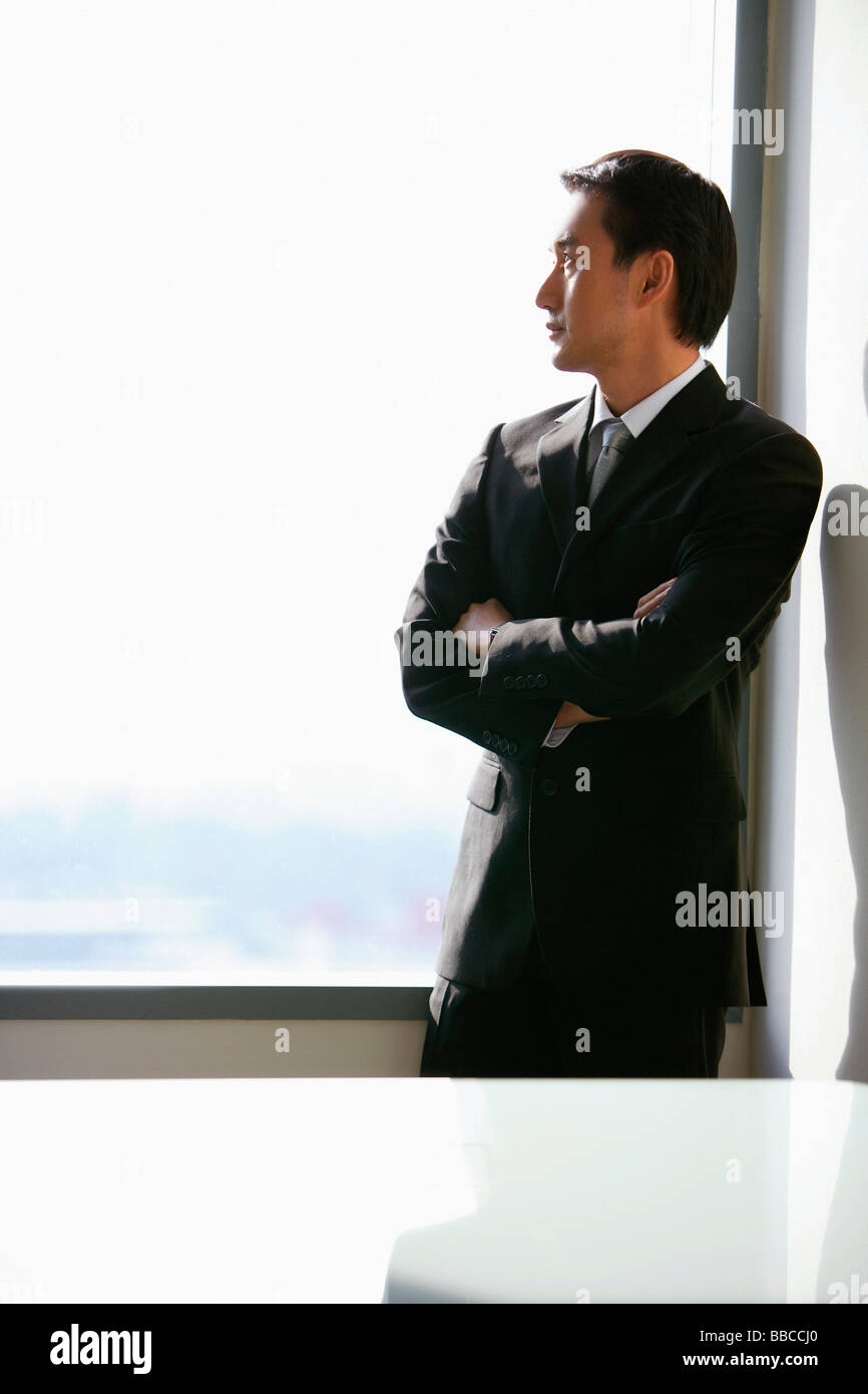 Businessman standing next to window, looking out, side view Stock Photo ...